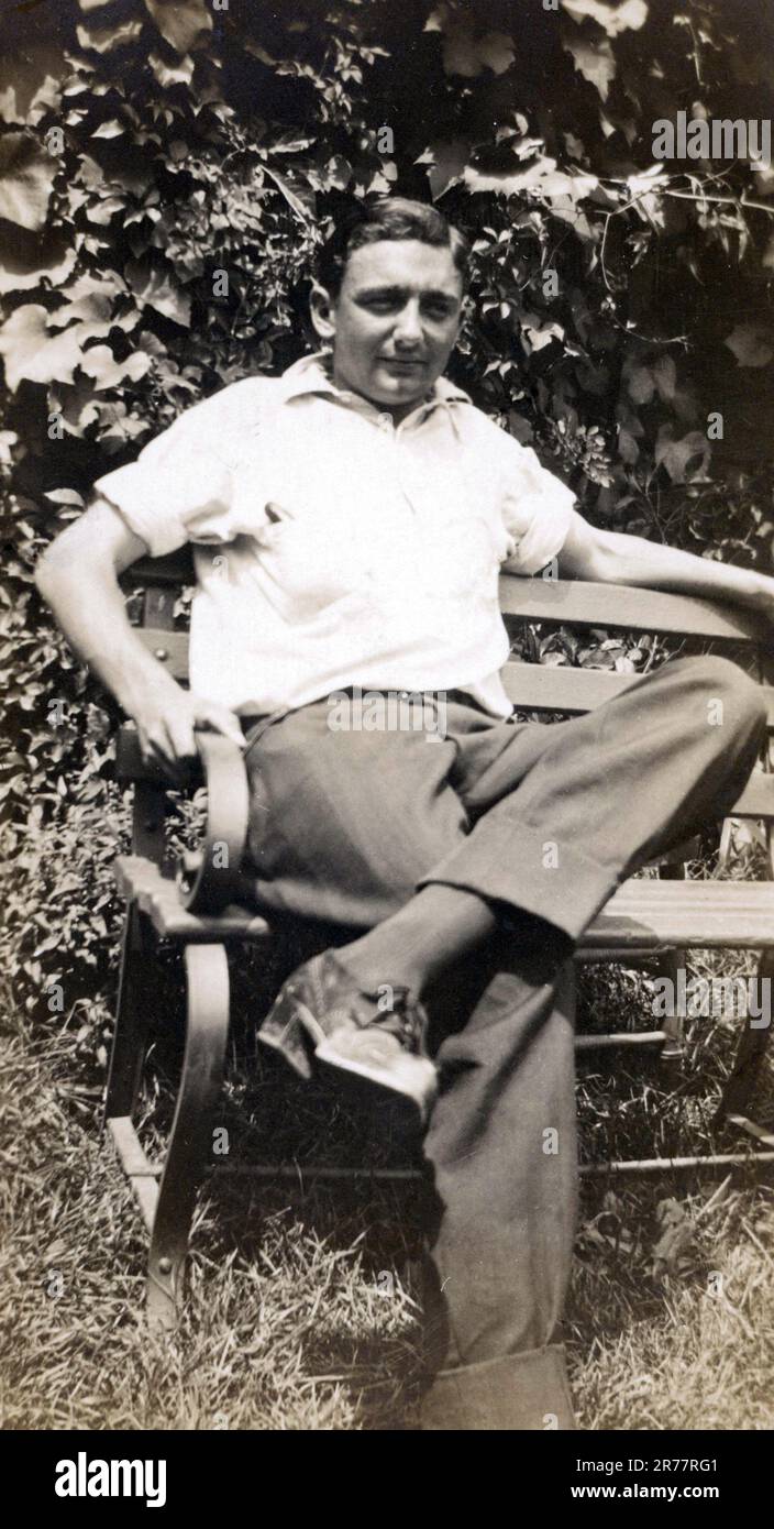 Vintage photographic postcard of a young man sitting outdoors on a park ...
