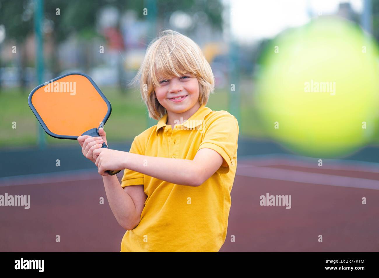 Happy blonde boy playing pickleball game, hitting pickleball yellow ...