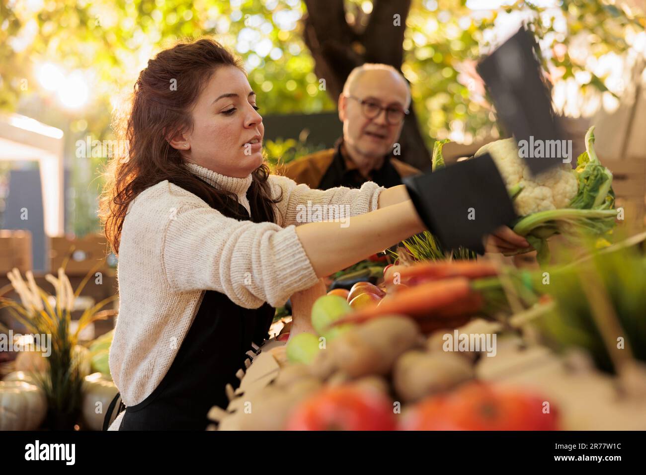 Senior person and young seller putting colorful produce on farmers ...