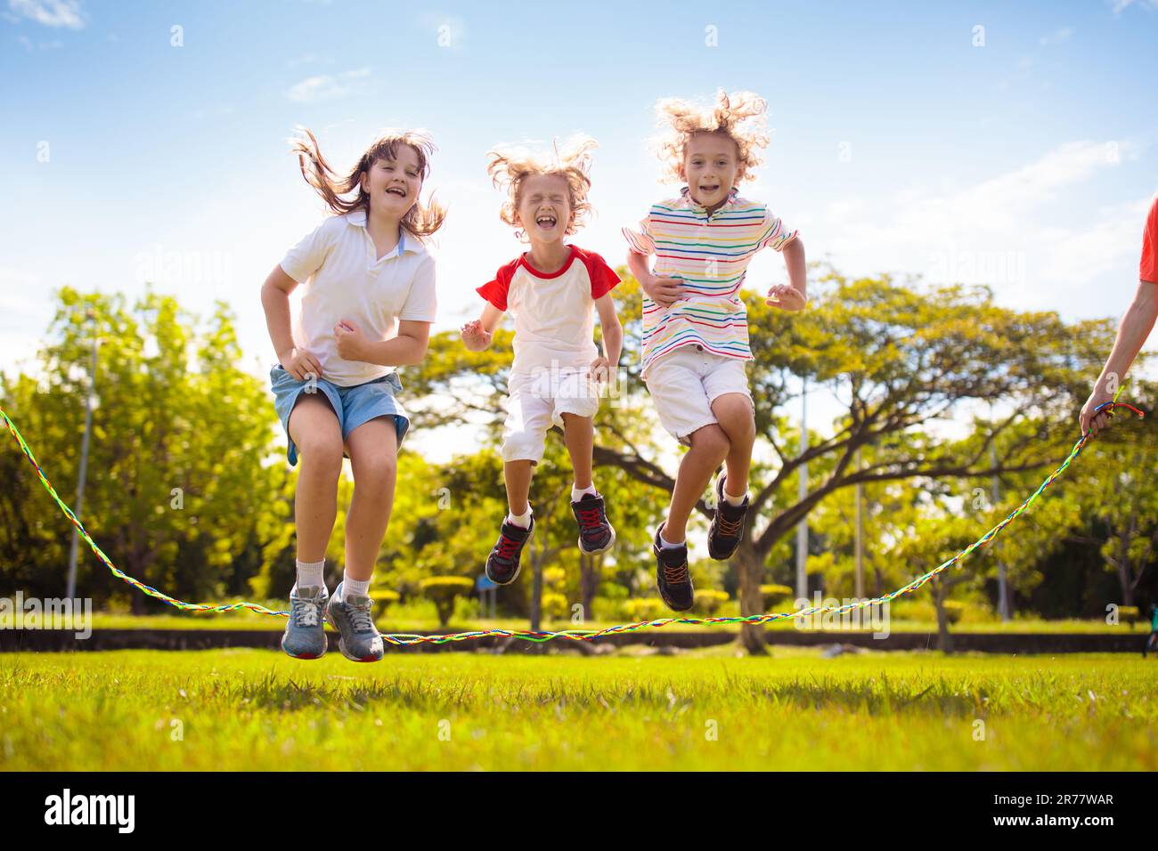Happy kids play outdoor. Children skipping rope in sunny garden. Summer holiday fun. Group of ...