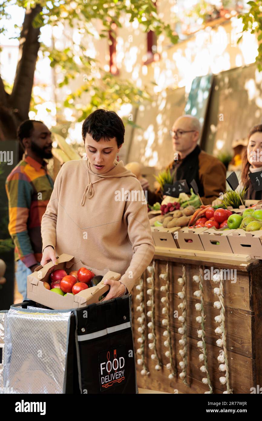 Young delivery girl putting fresh organic produce box in thermo bag ...