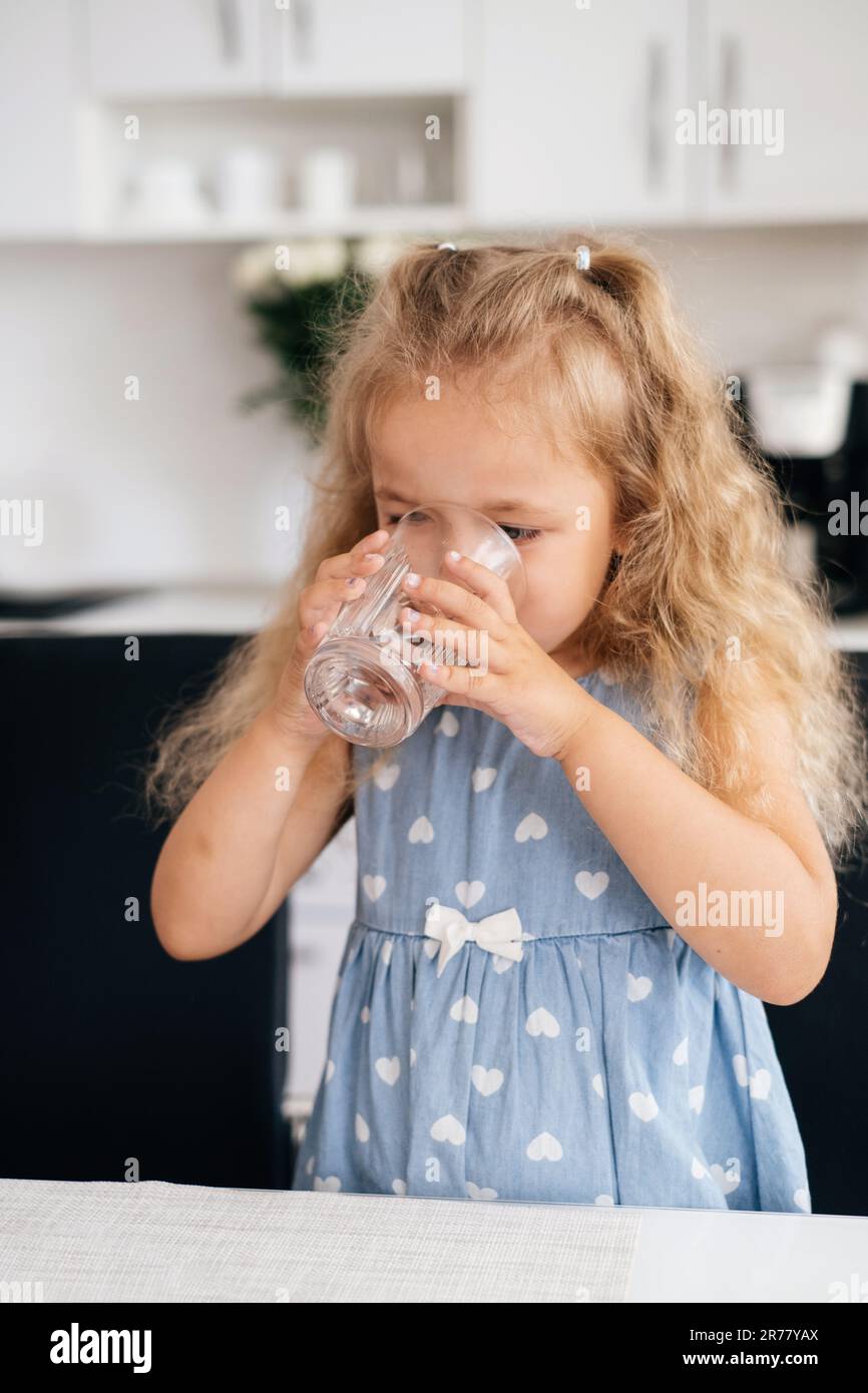 Toddler child drinking water at home from the glass on the kitchen. Kid ...