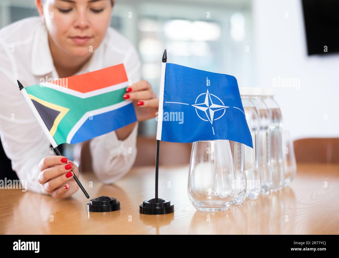 Young woman putting South Africa and NATO flags on table in office ...