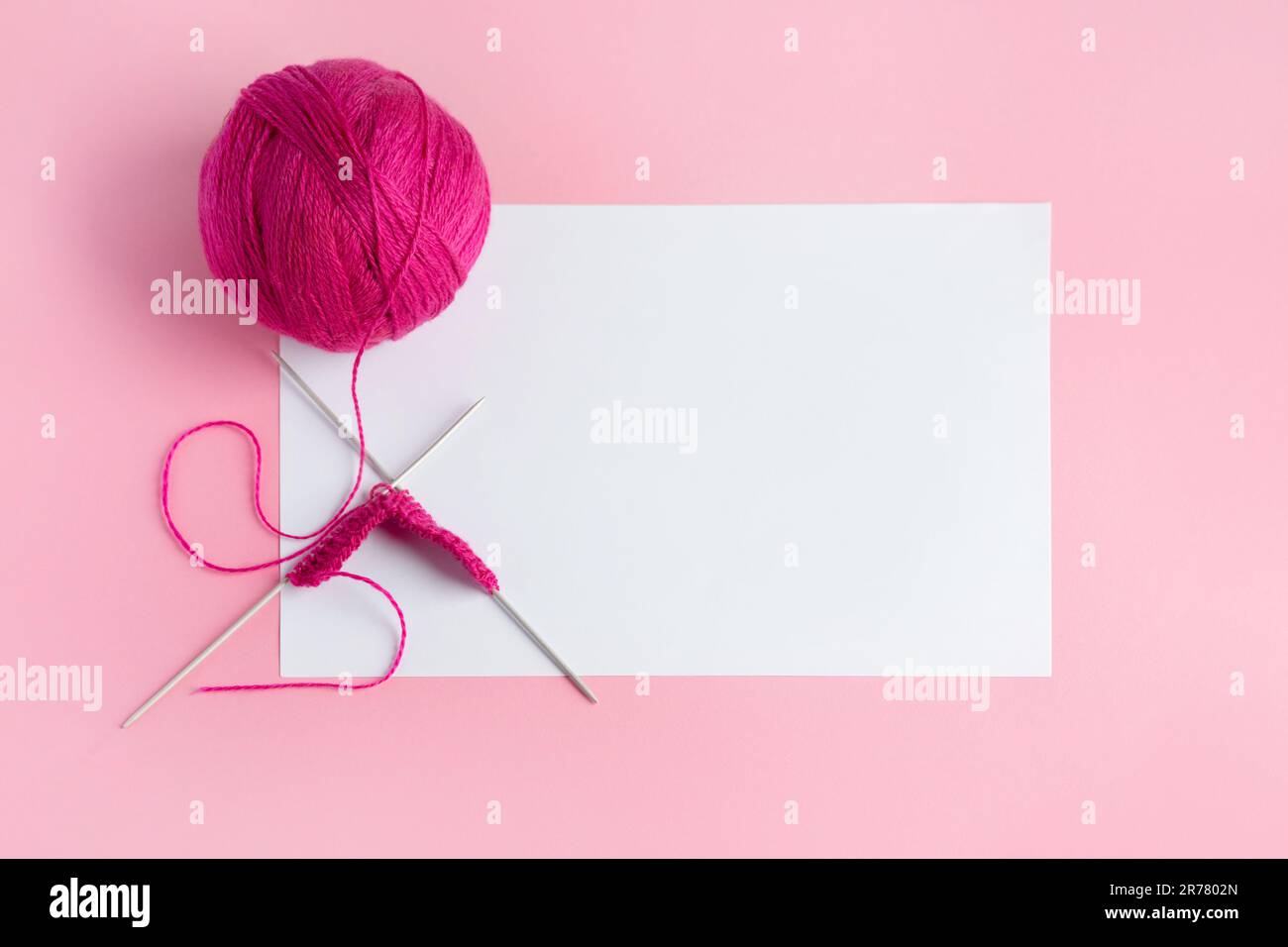 Pink ball of thread and knitting needles with a white sheet of paper ...