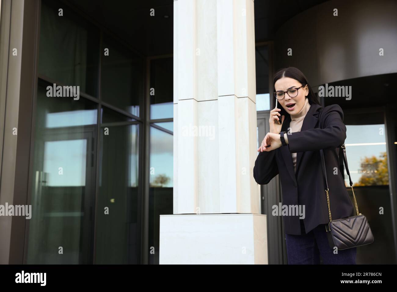 Emotional woman checking time while talking on smartphone outdoors ...