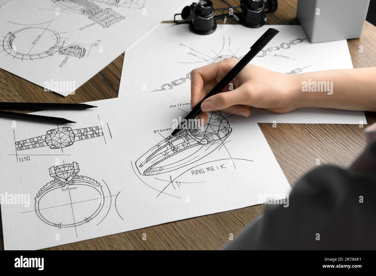 Jeweler drawing sketch of elegant ring on paper at wooden table ...