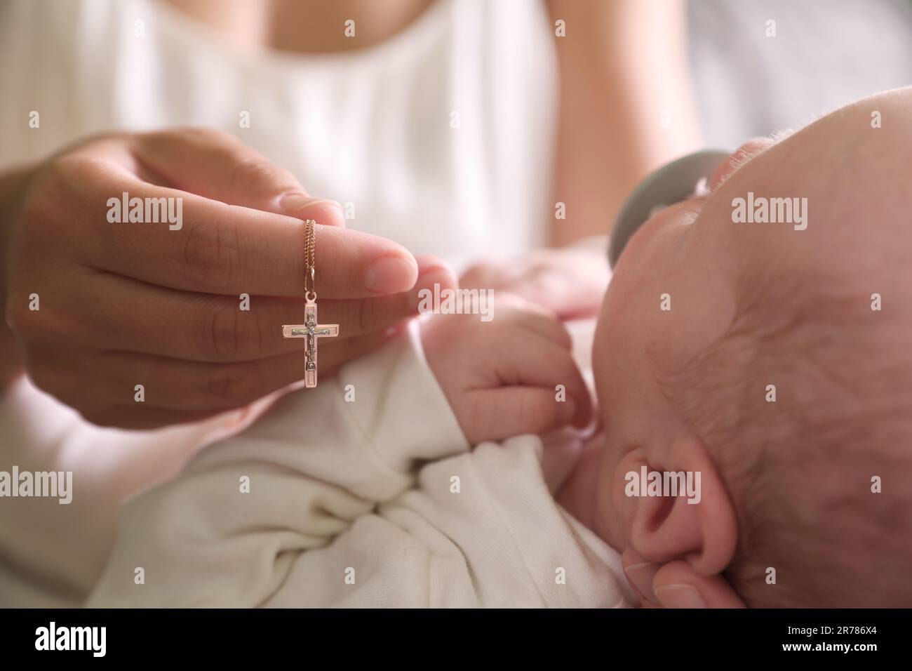 Mother holding Christian cross near newborn baby indoors, focus on hand ...