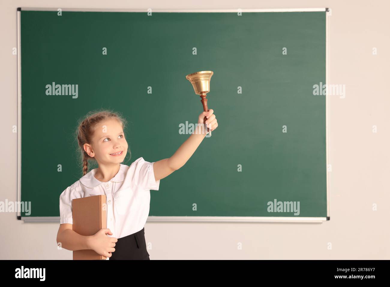 Pupil with school bell near chalkboard in classroom, space for text ...