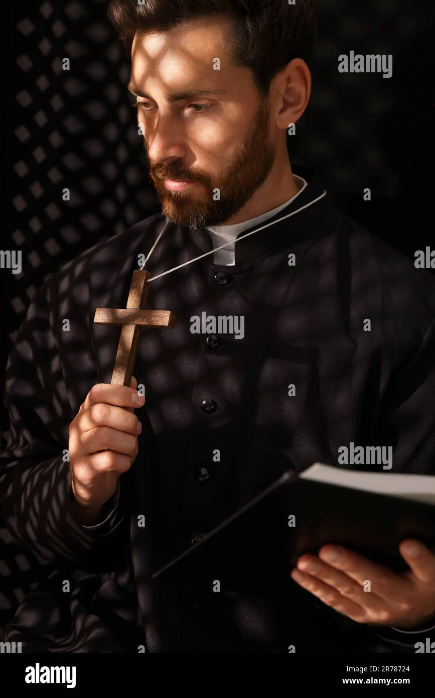 Catholic priest in cassock holding cross with Bible in confessional ...