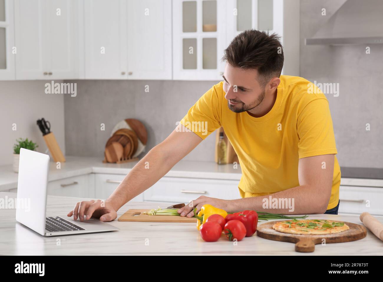 Man watching cooking online course on laptop while making pizza in ...