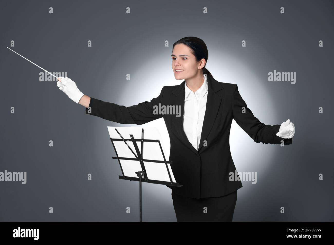 Happy professional conductor with baton and note stand on grey ...