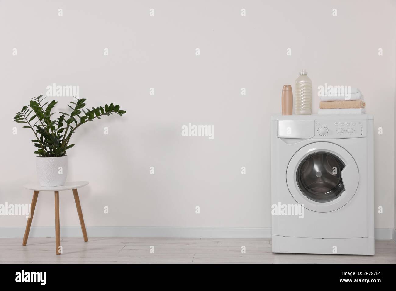 Modern washing machine and potted plant on stool against white wall ...