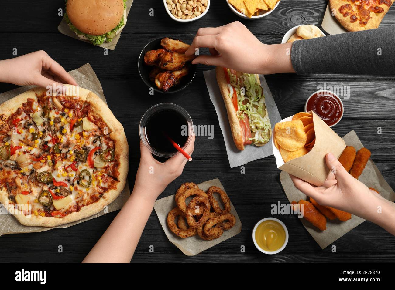 Friends eating pizza, chicken wings and other fast food at black wooden ...