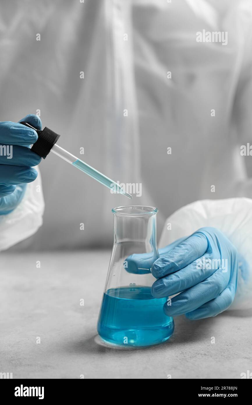 Scientist dripping liquid from pipette into beaker at white table ...