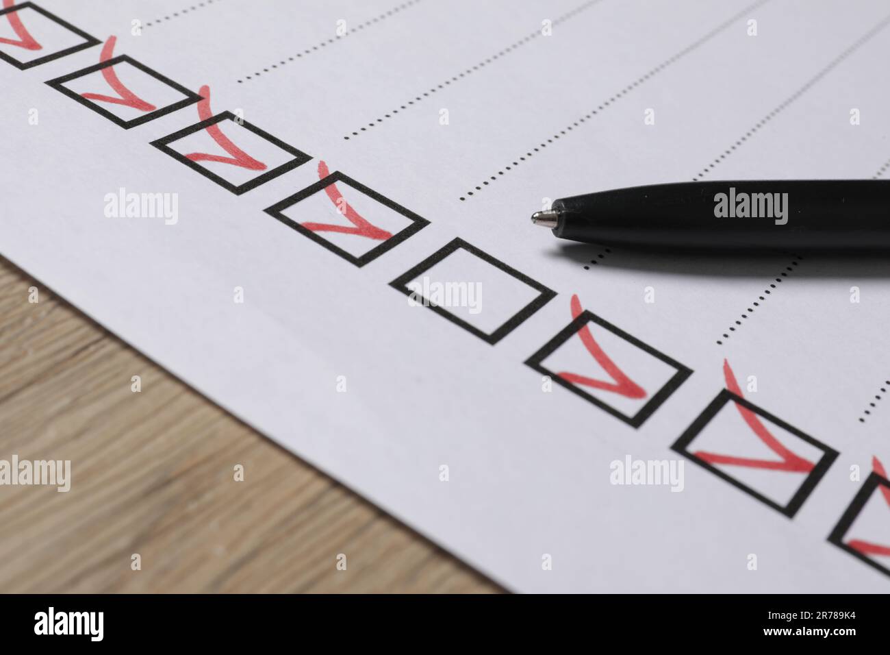 Paper sheet with checkboxes and pen on wooden table, closeup. Checklist ...
