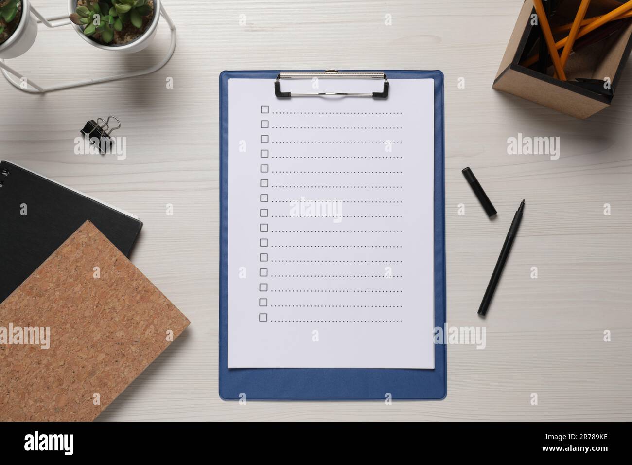 Clipboard with checkboxes, plant and office stationery on white wooden ...