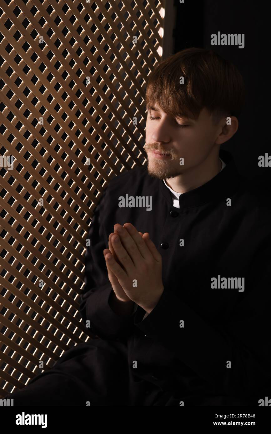 Catholic priest praying near wooden partition in confessional Stock ...
