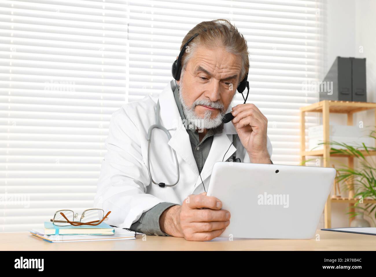 Senior doctor with tablet consulting patient at wooden desk in clinic ...