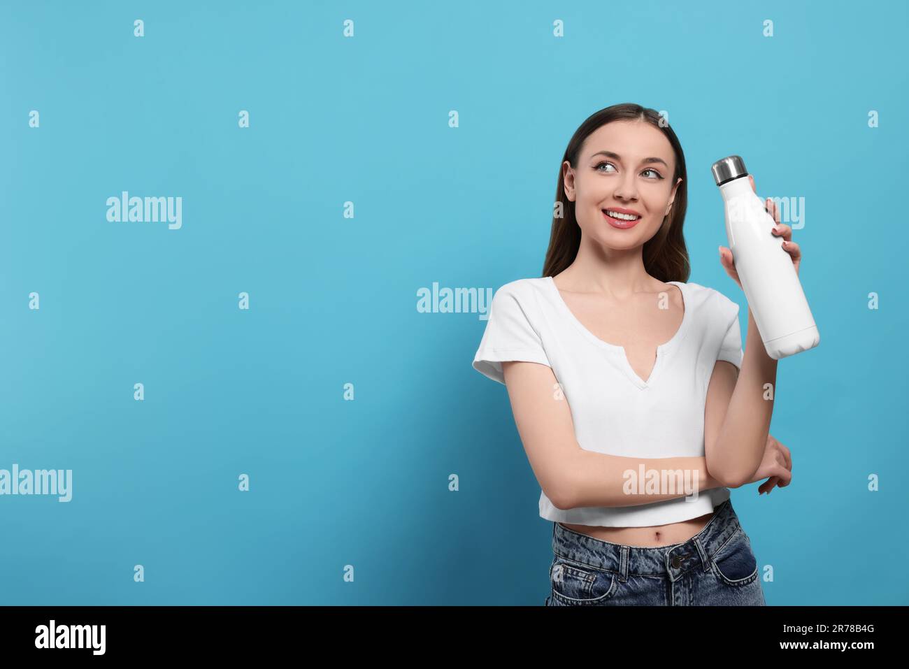 Beautiful young woman with thermos bottle on light blue background ...