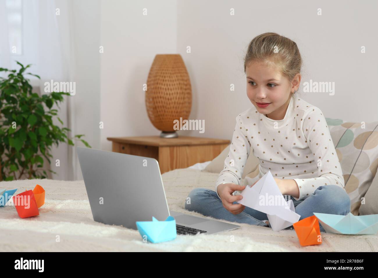 Little girl learning to make paper boats with online course at home ...