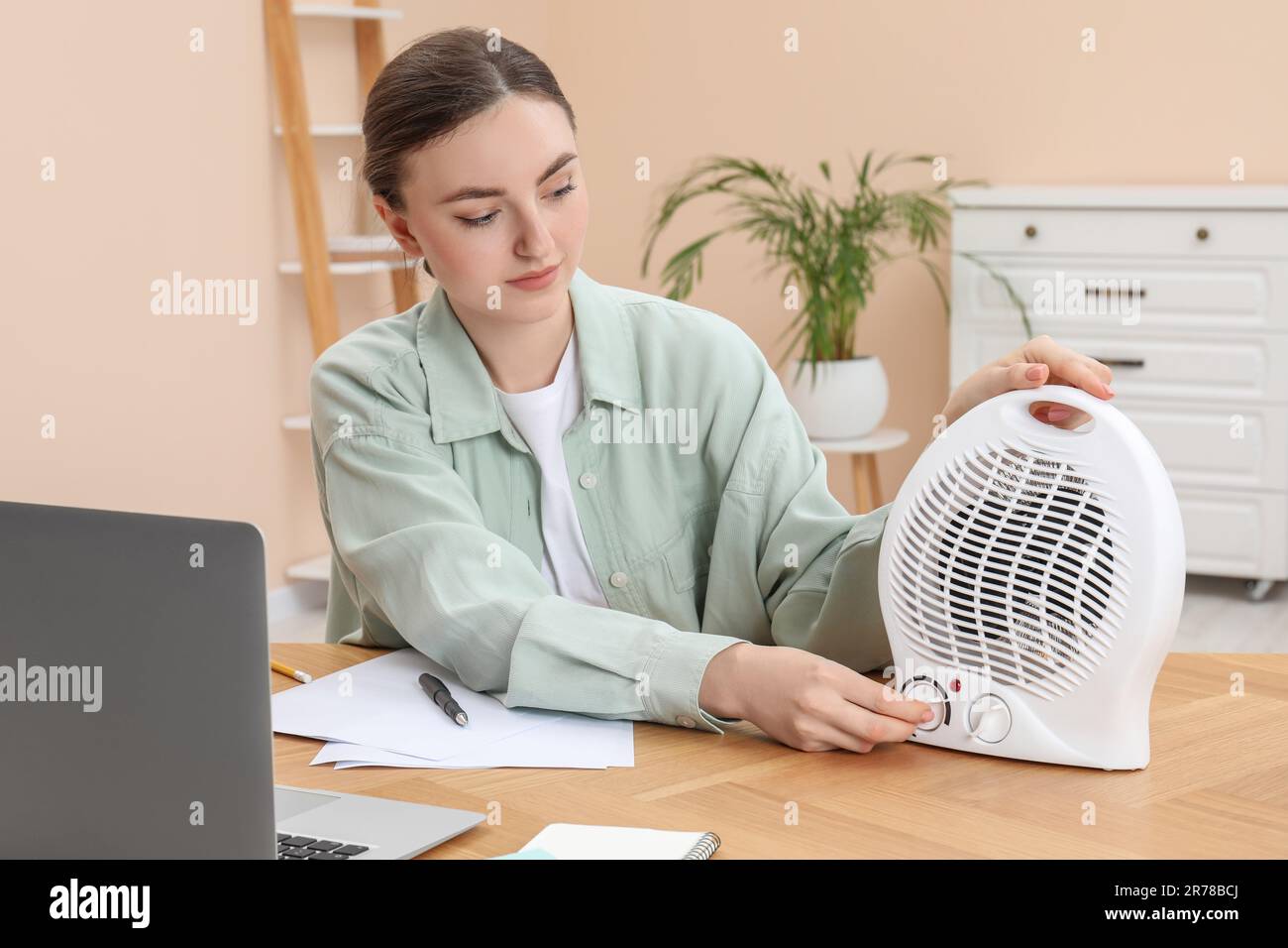 Young woman adjusting temperature on modern electric fan heater at ...