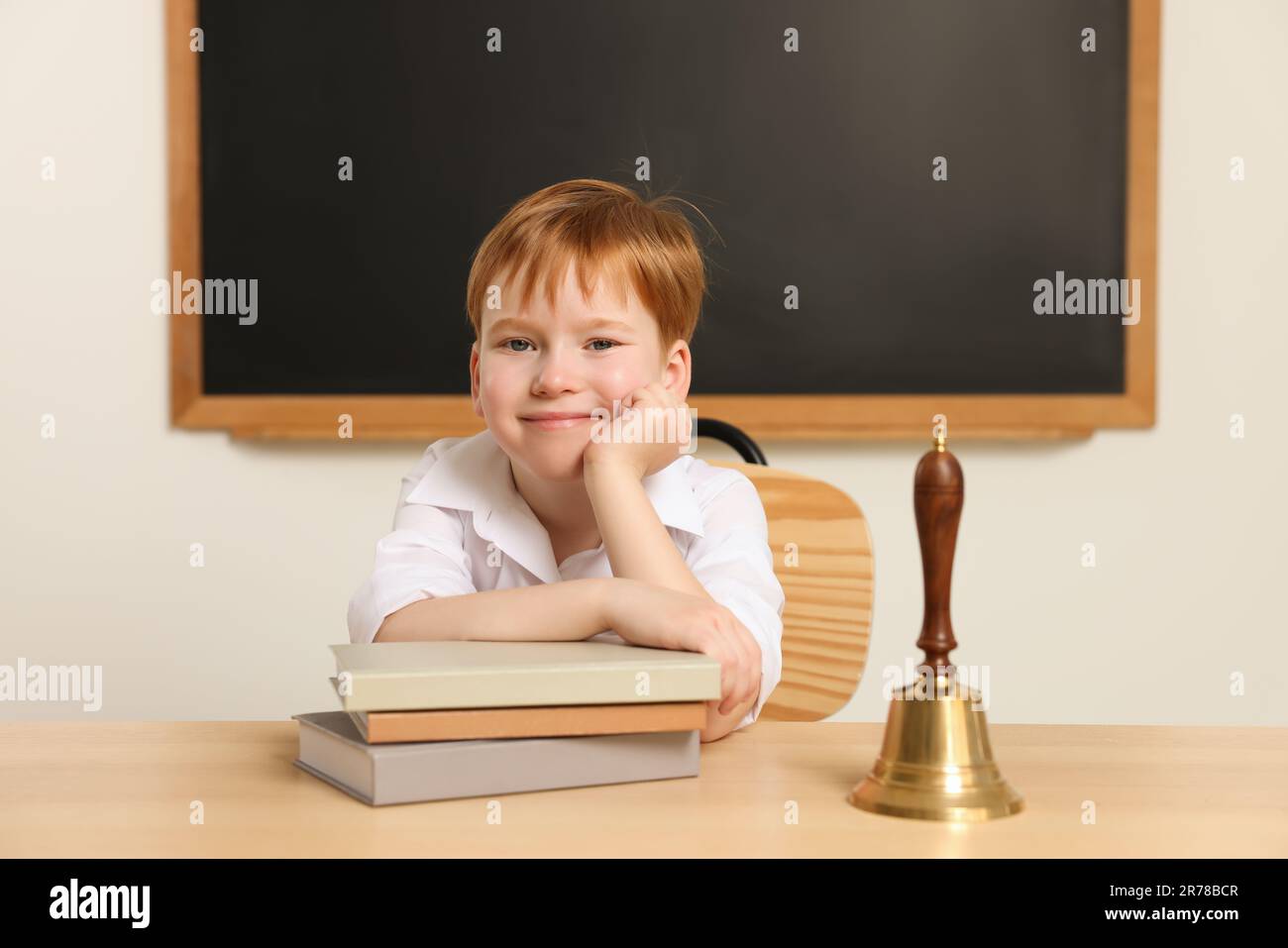 Cute little boy with books and school bell in classroom Stock Photo - Alamy