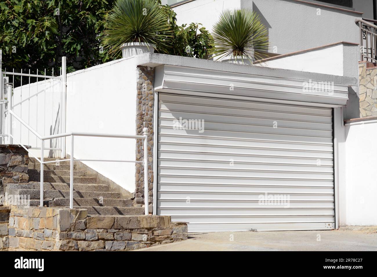 Building with white roller shutter garage door, stairs and gate ...