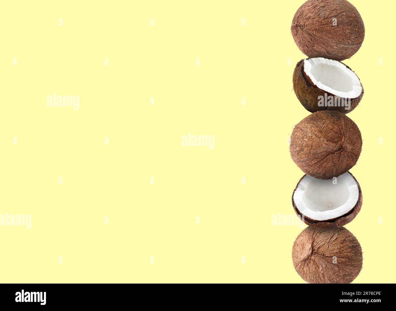 Stack of fresh coconuts on pale light yellow background. Space for text ...