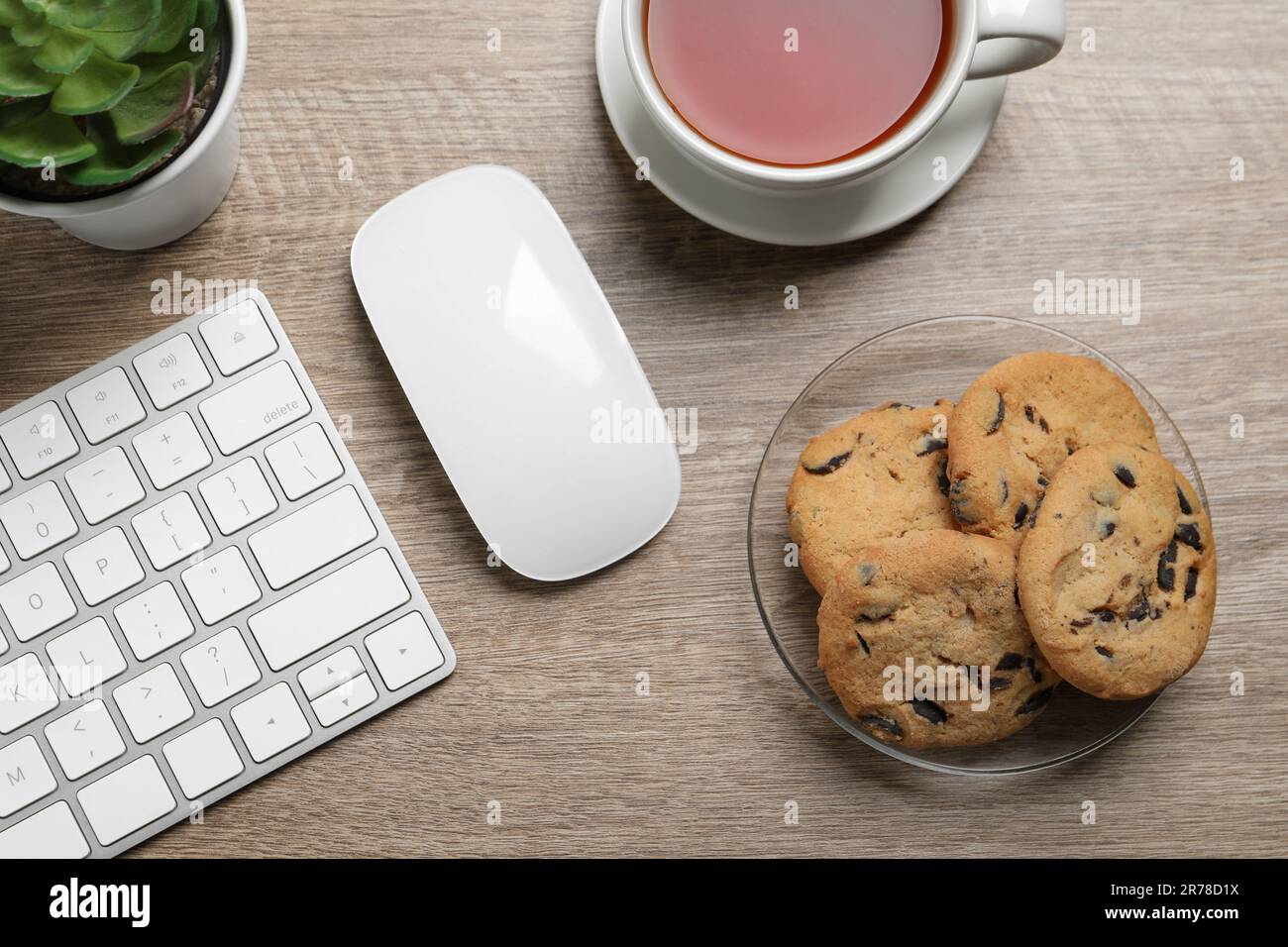 Chocolate chip cookies, tea and keyboard on wooden table at workplace ...