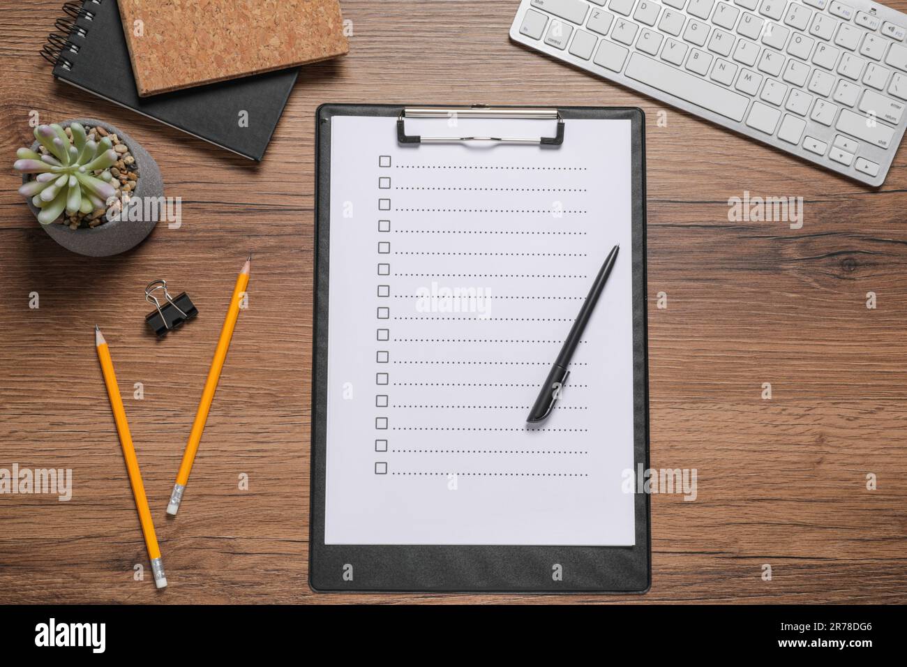 Clipboard with checkboxes, computer keyboard and plant on wooden table ...