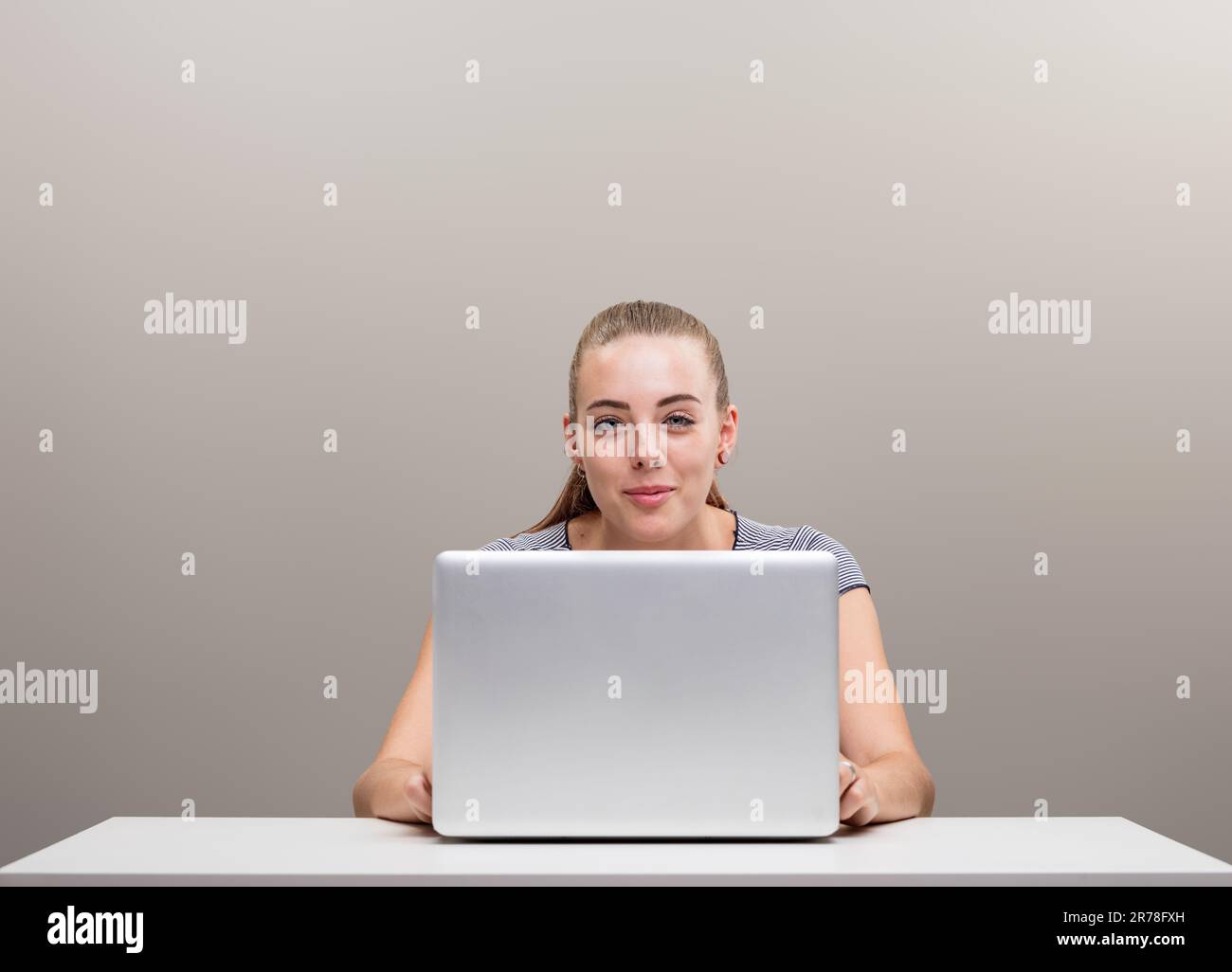 A gorgeous young woman at a desk, joyfully engaged with her laptop ...