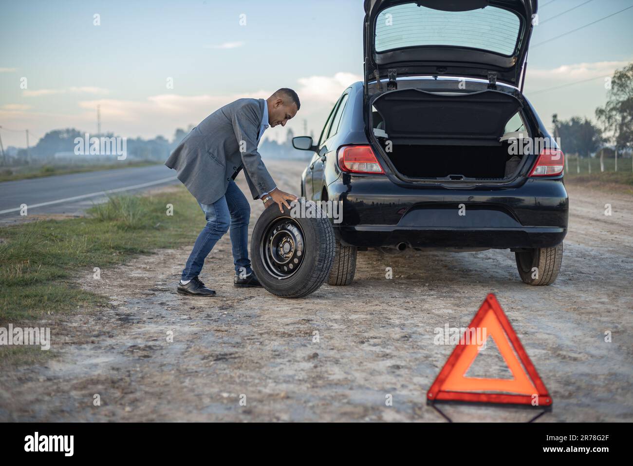 Latino man changes a flat tire on his car at the side of the road Stock ...