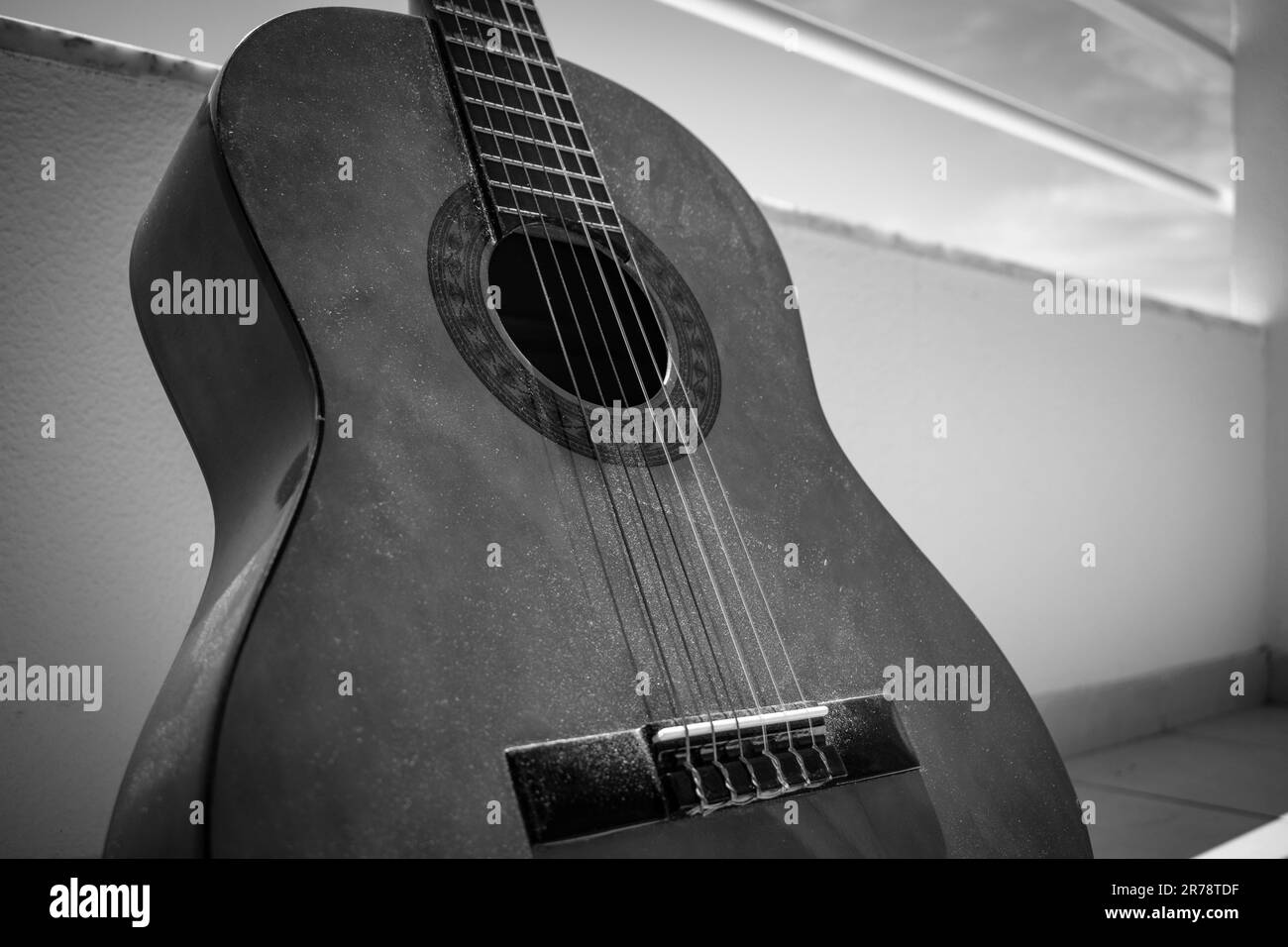A grayscale of an acoustic guitar leaning against a white wall in front ...