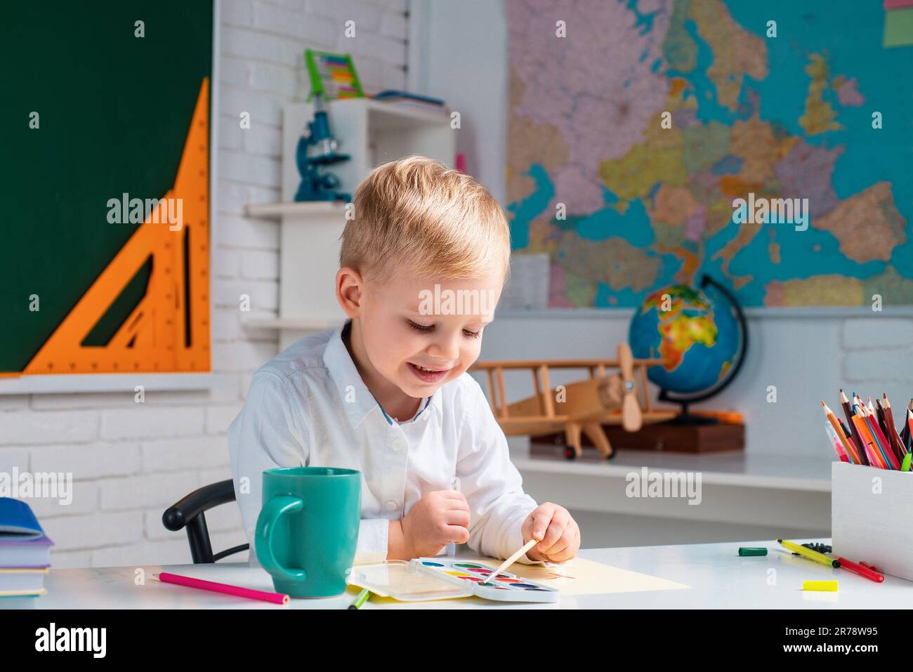 Pupil child is sitting at a desk indoors. Cute pupil with funny face ...