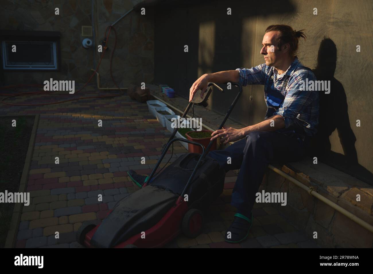 Portrait of a tired overworked gardener man with electric lawn mower ...