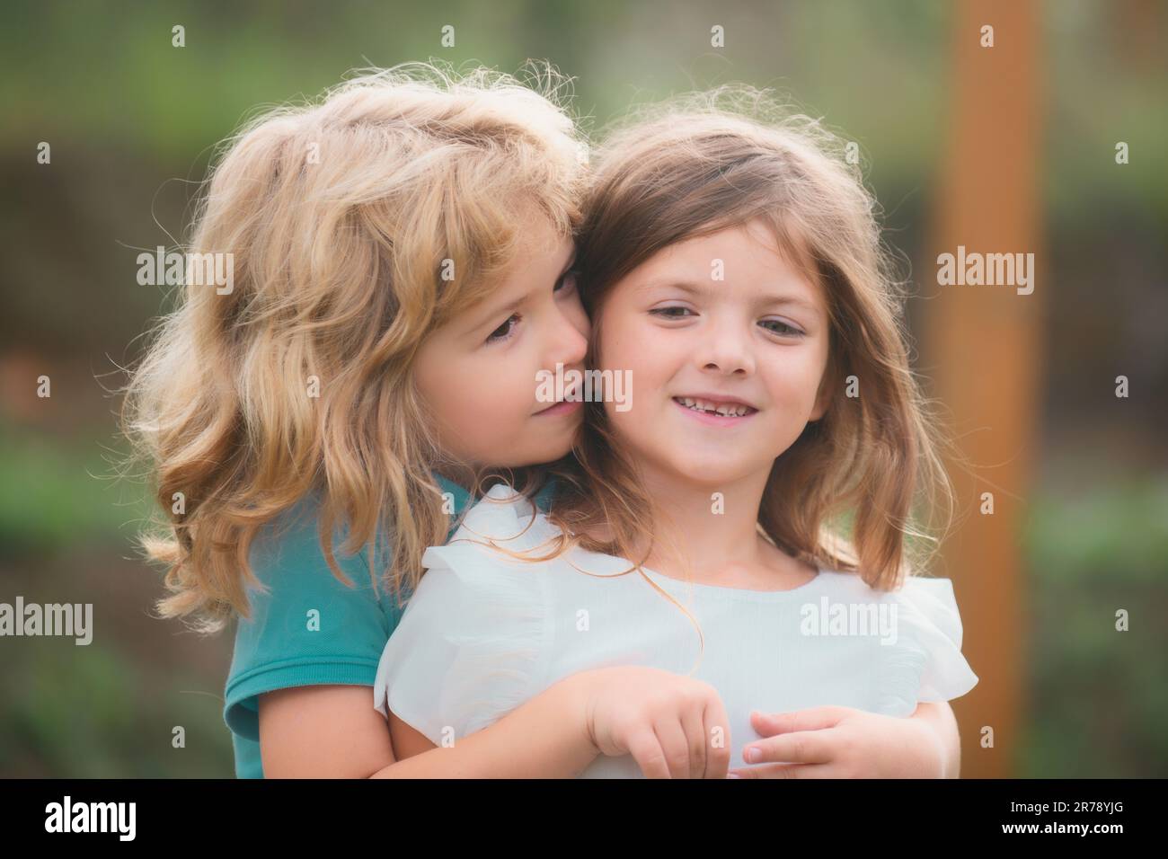 Two little children hug and kiss each other in summer garden. Kids ...