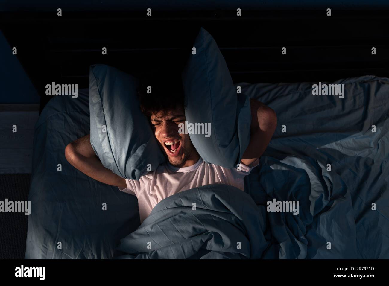 Irritated young man laying in bed at night, covering his head with ...