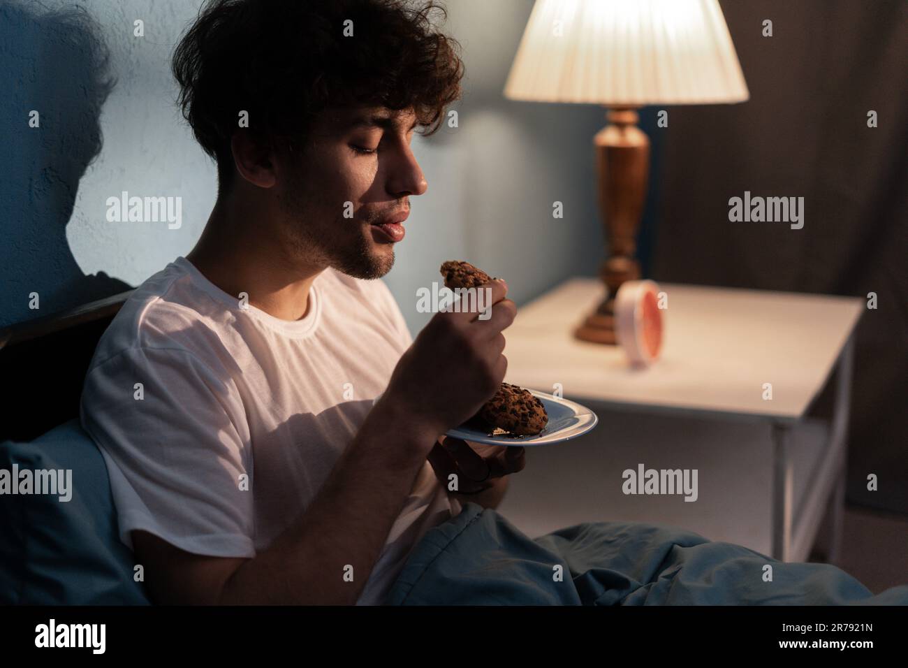 Stressed young man having a cookies at night. Unhappy tired depressed ...