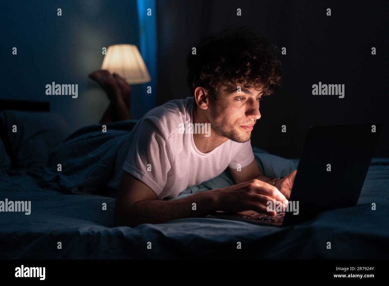 Young internet addict man networking concentrated late at night on bed ...