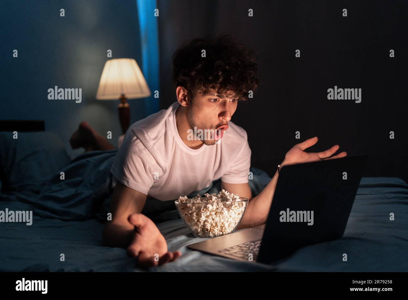 Amazed guy eating popcorn and watching horror movie on laptop while ...