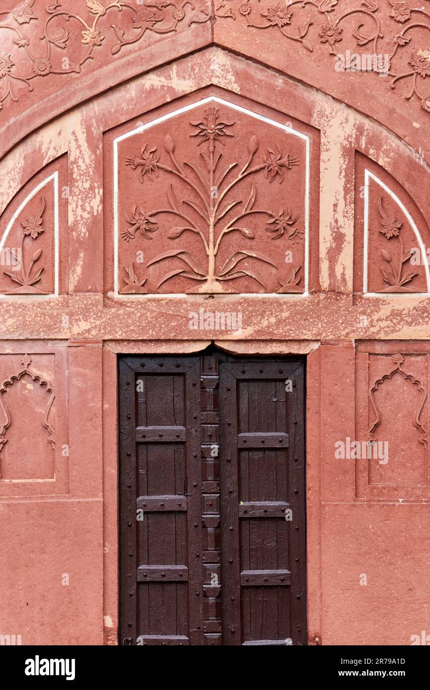 Decorative flowers on red sandstone wall of Taj Mahal above old wooden ...