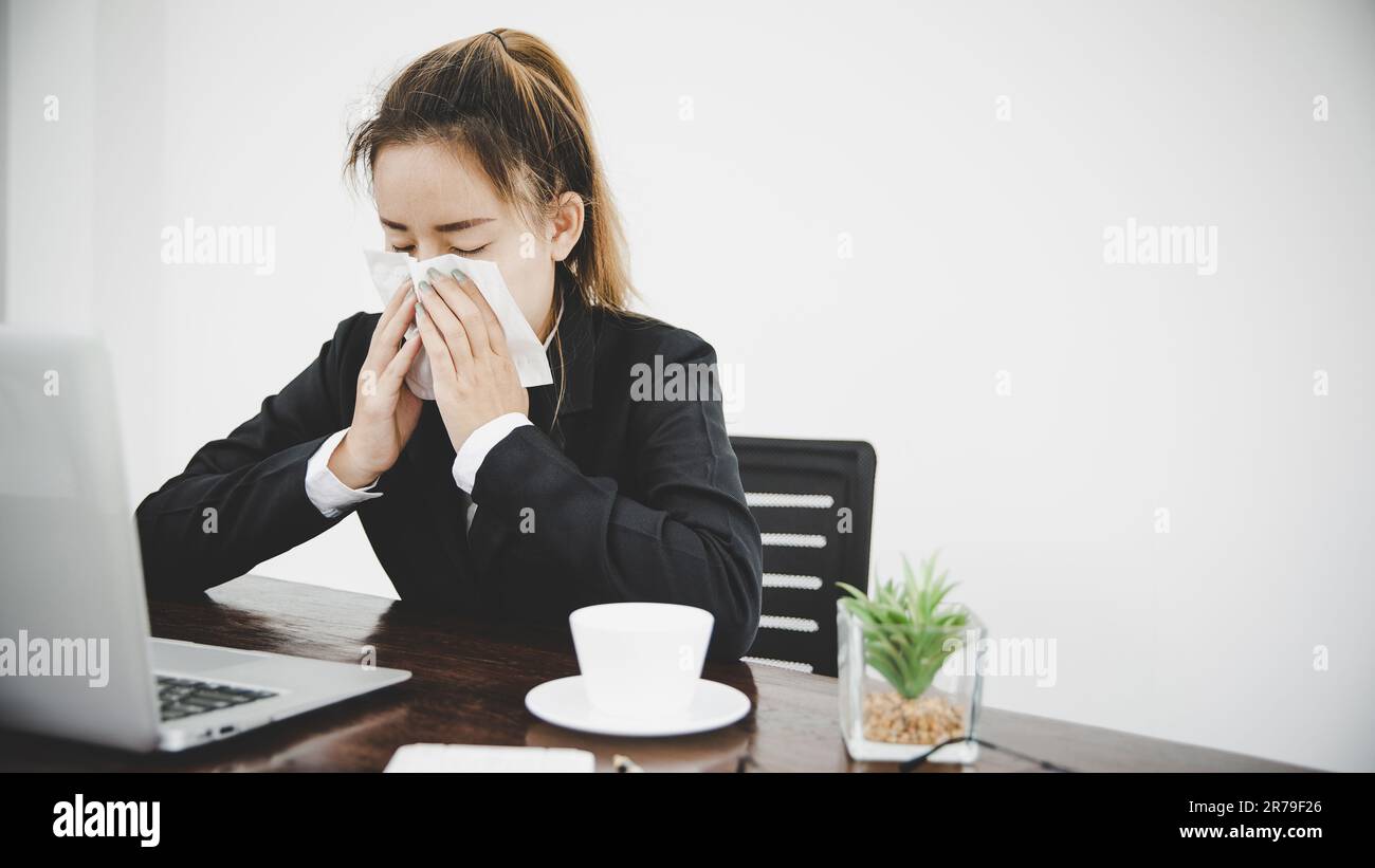 Sick young asian business woman sitting alone at work sneeze holding ...