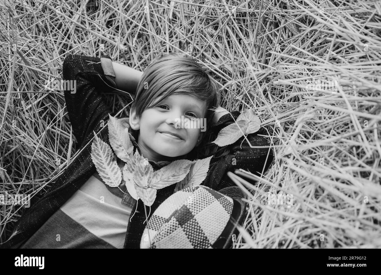 Smiling little boy playing with leaves and looking at camera. Kid boy ...