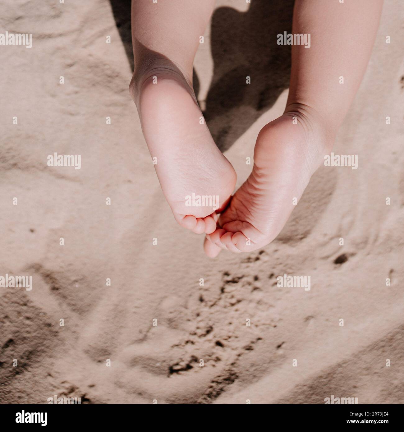 An adorable close-up of a baby's feet reaching out amongst the sand and ...