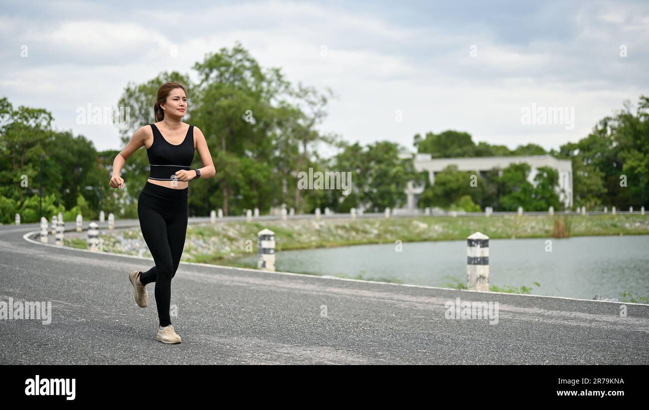 An attractive and healthy Asian female runner in sportswear is running ...