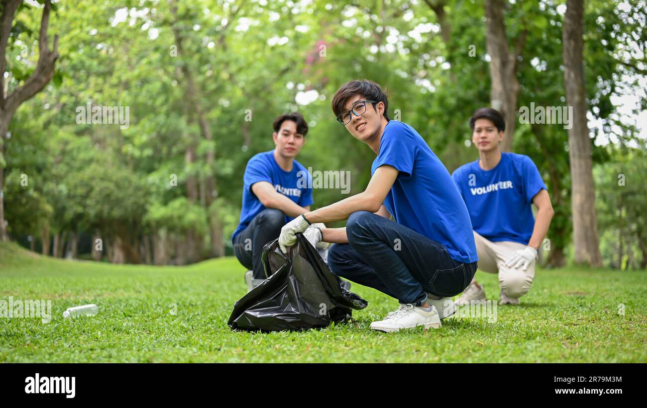 A happy young Asian male volunteer with a plastic garbage bag cleans up ...