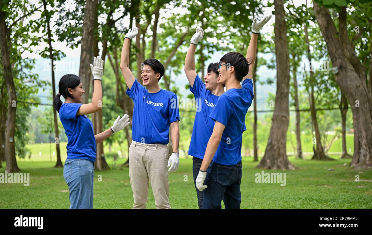 A group of cheerful young Asian volunteers in uniform raised their ...