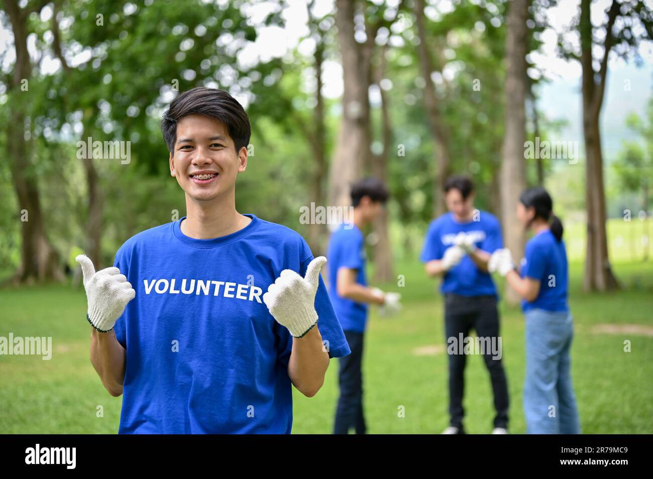 A happy young Asian male volunteer stands in a public park and shows ...