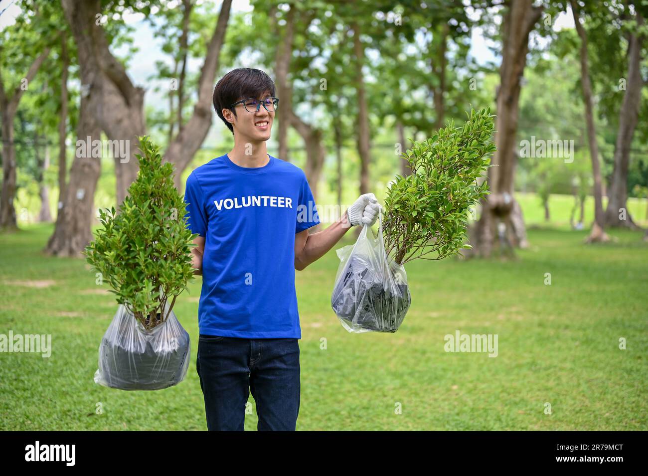 A happy young Asian male volunteer walks with plants in his hands ...