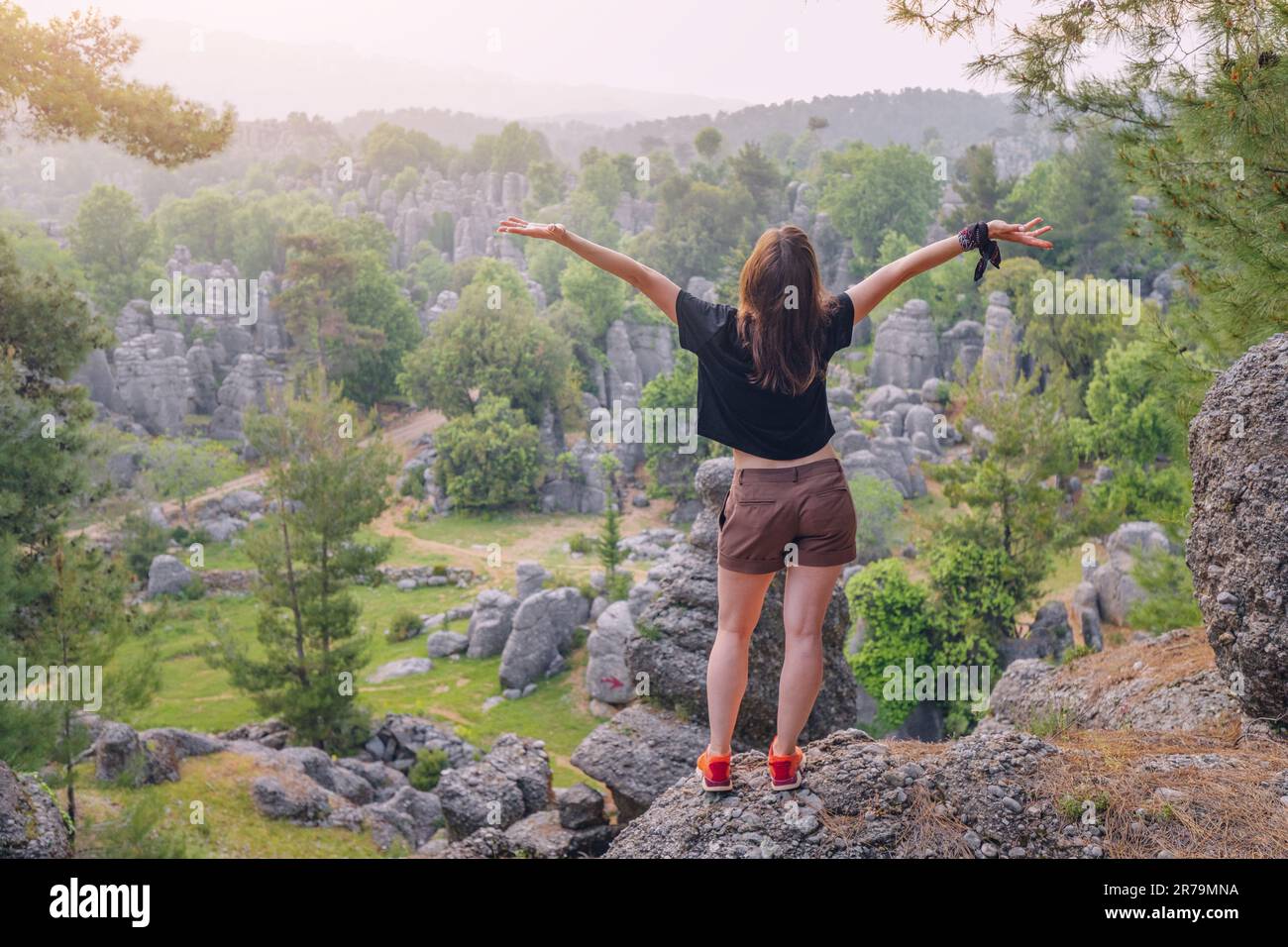 Happy traveler girl standing on top of the rock cliff with view of stone remnants in Altinkaya ...